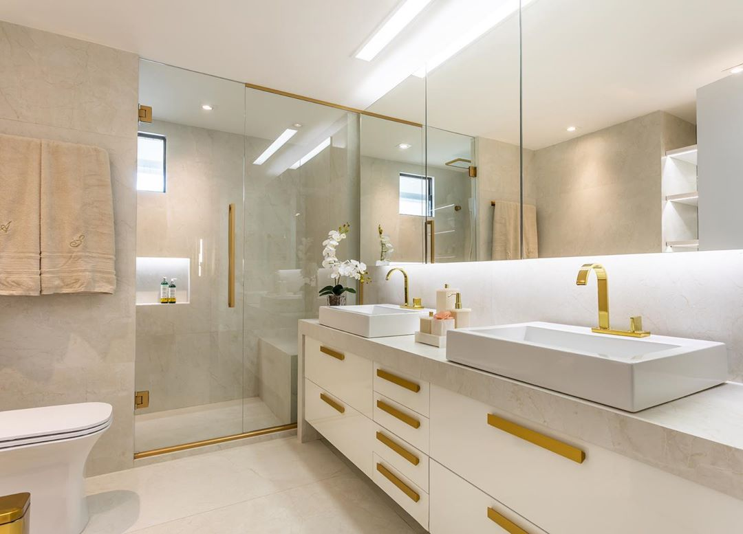 Banheiro com cores claras e detalhes dourados revestido com porcelanato ...