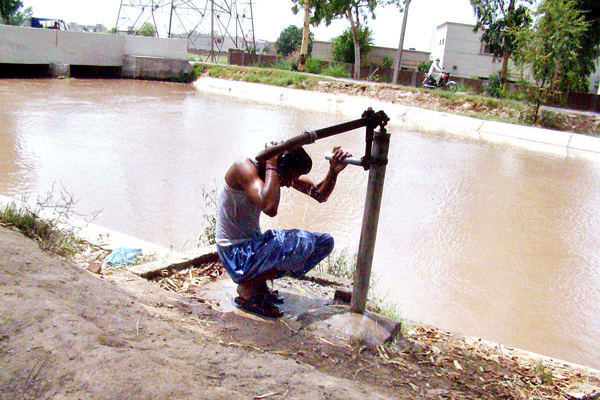 A person bathing under a hand pump to get some relief from scorching ...