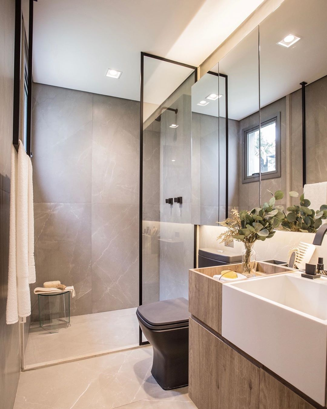 Banheiro pequeno preto e cinza com nichos na bancada e box uma folha ...